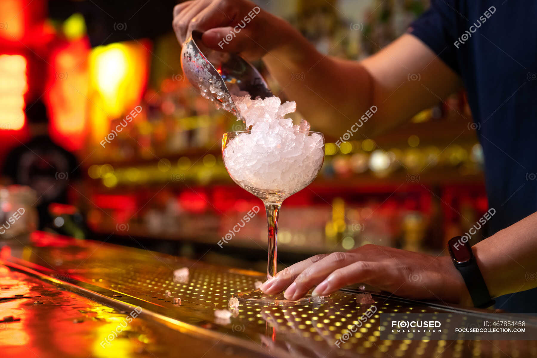 Hands of unrecognizable bartender putting crushed ice into the cup while preparing a cocktail in ...