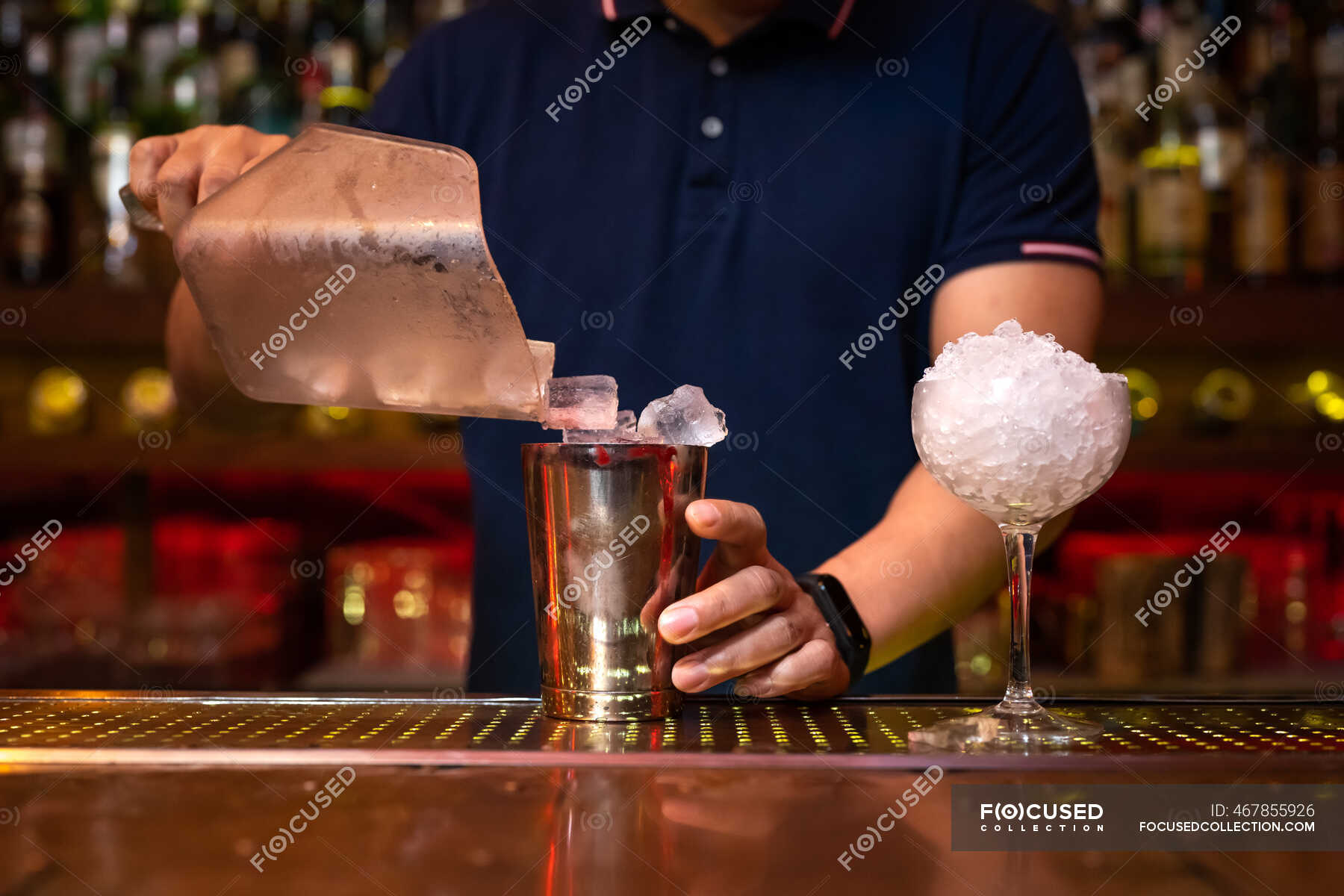 Hands of unrecognizable bartender putting ice cubes into the shaker while preparing a cocktail ...
