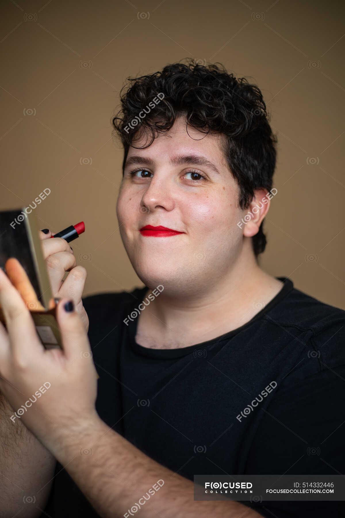 Feminine Androgynous Man With Curly Hair Applying Lipstick On Lips