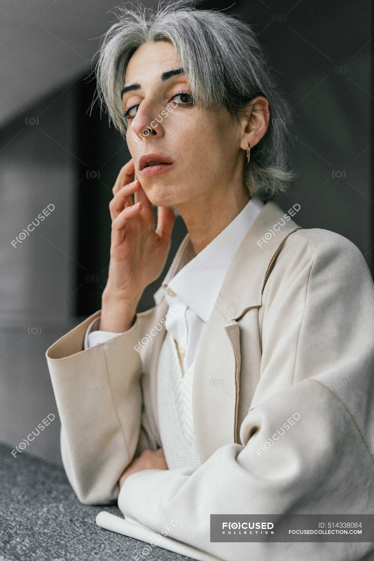 Serious Transgender Female In Trendy Coat Leaning On Gray Fence While Standing In Street Looking