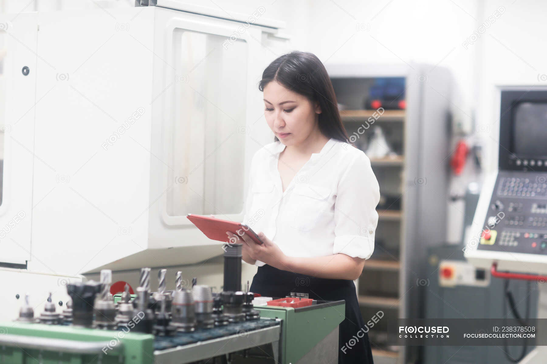 Portrait of a female engineer standing in a workshop holding a digital ...